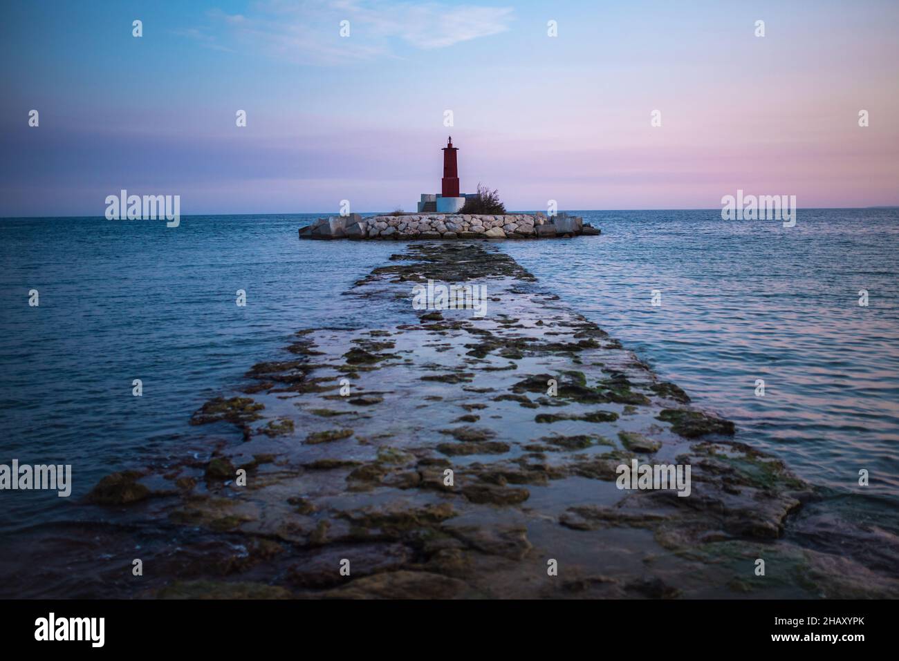 Long stony path half covered in water leading to red beacon on small ...
