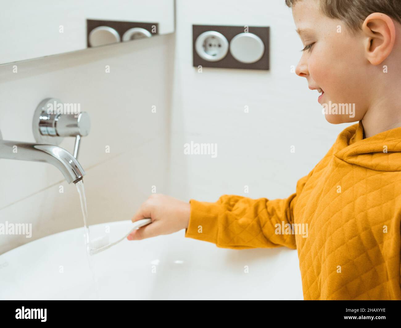 Cute boy in casual wear rinsing toothbrush while brushing teeth in ...