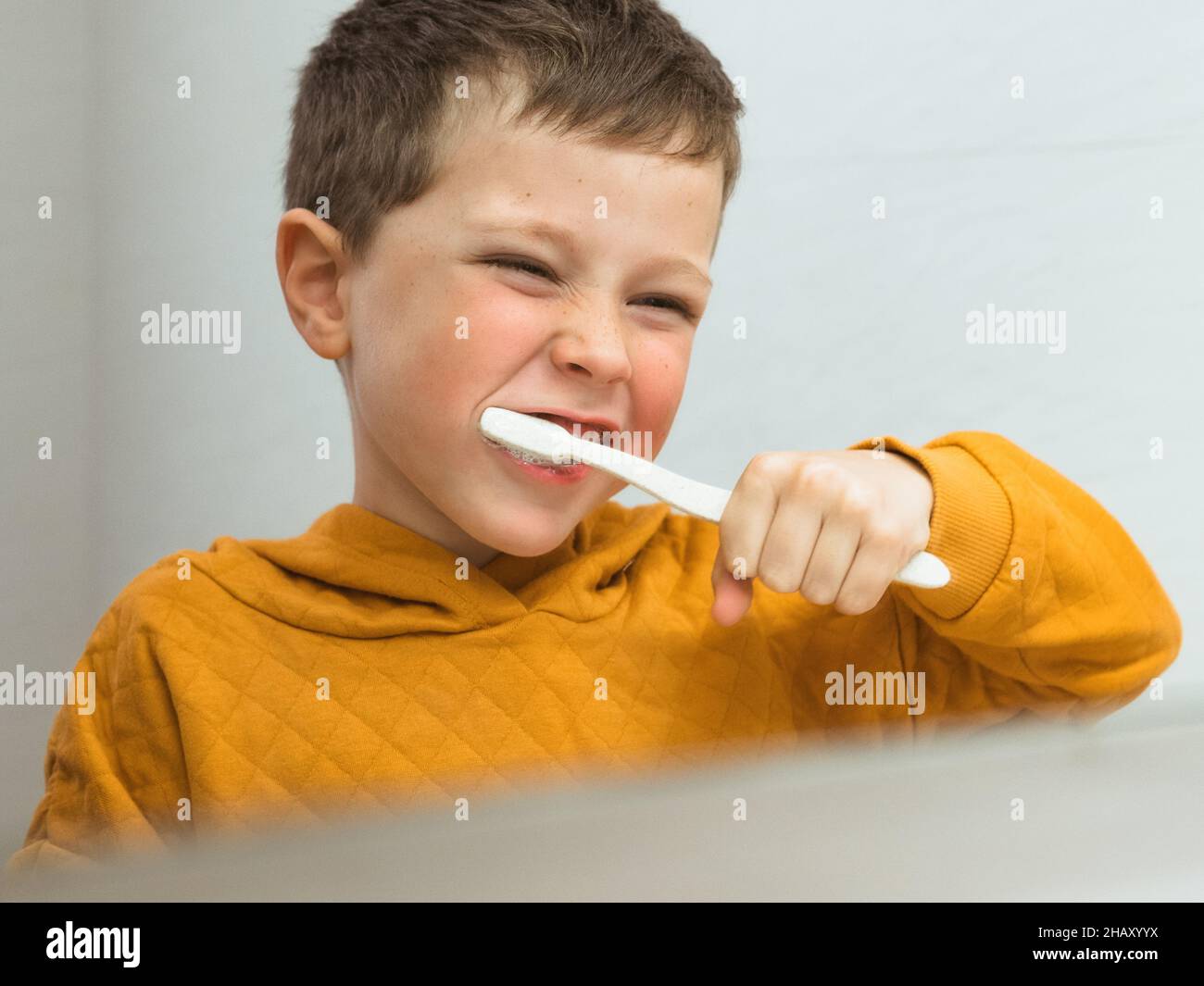 Cute boy in casual wear brushing teeth while looking at mirror standing ...