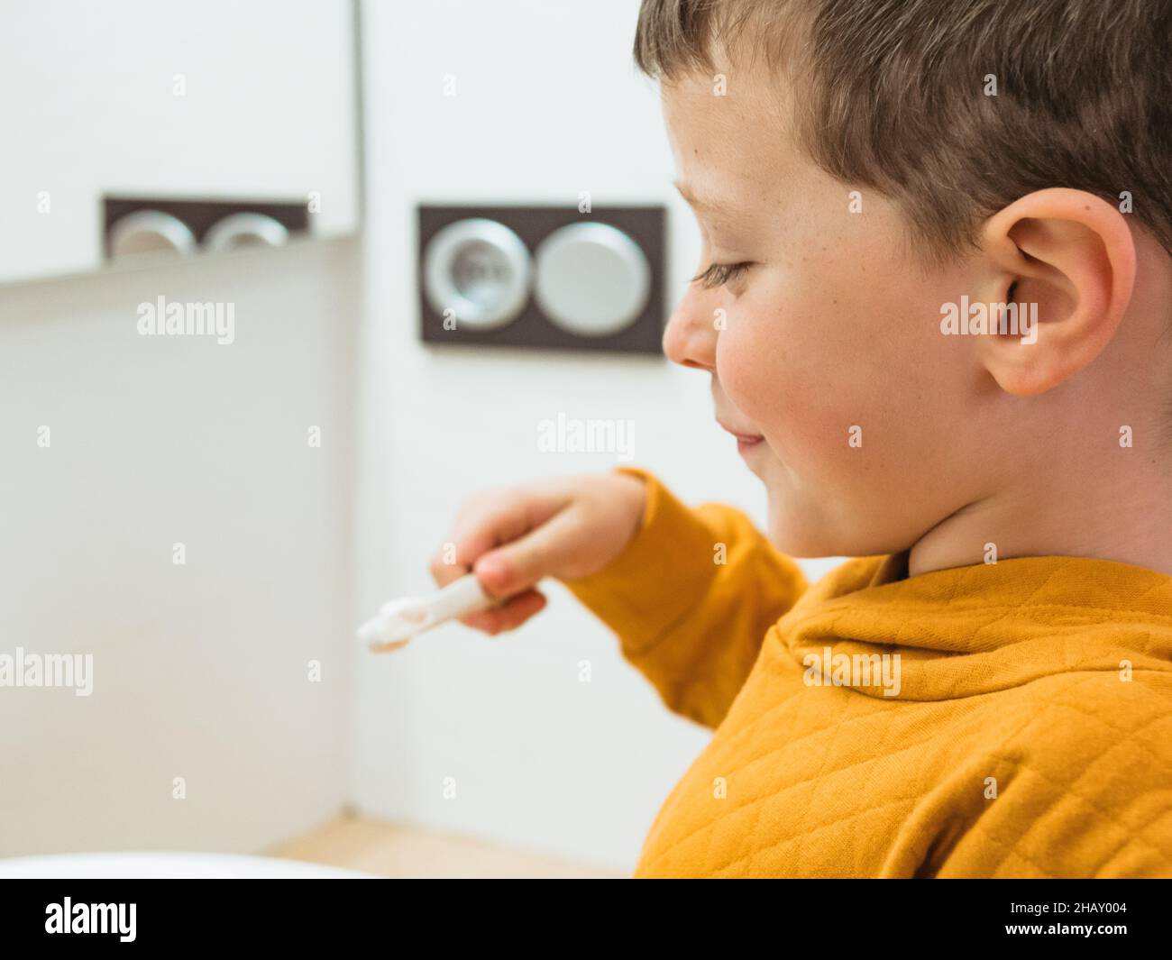 Cute boy in casual wear brushing teeth in bathroom during morning ...
