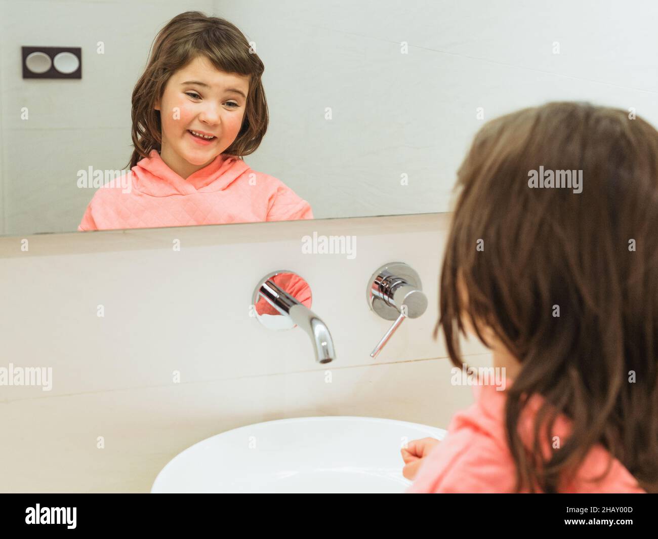 Positive girl looking at mirror while standing at sink with taps in ...