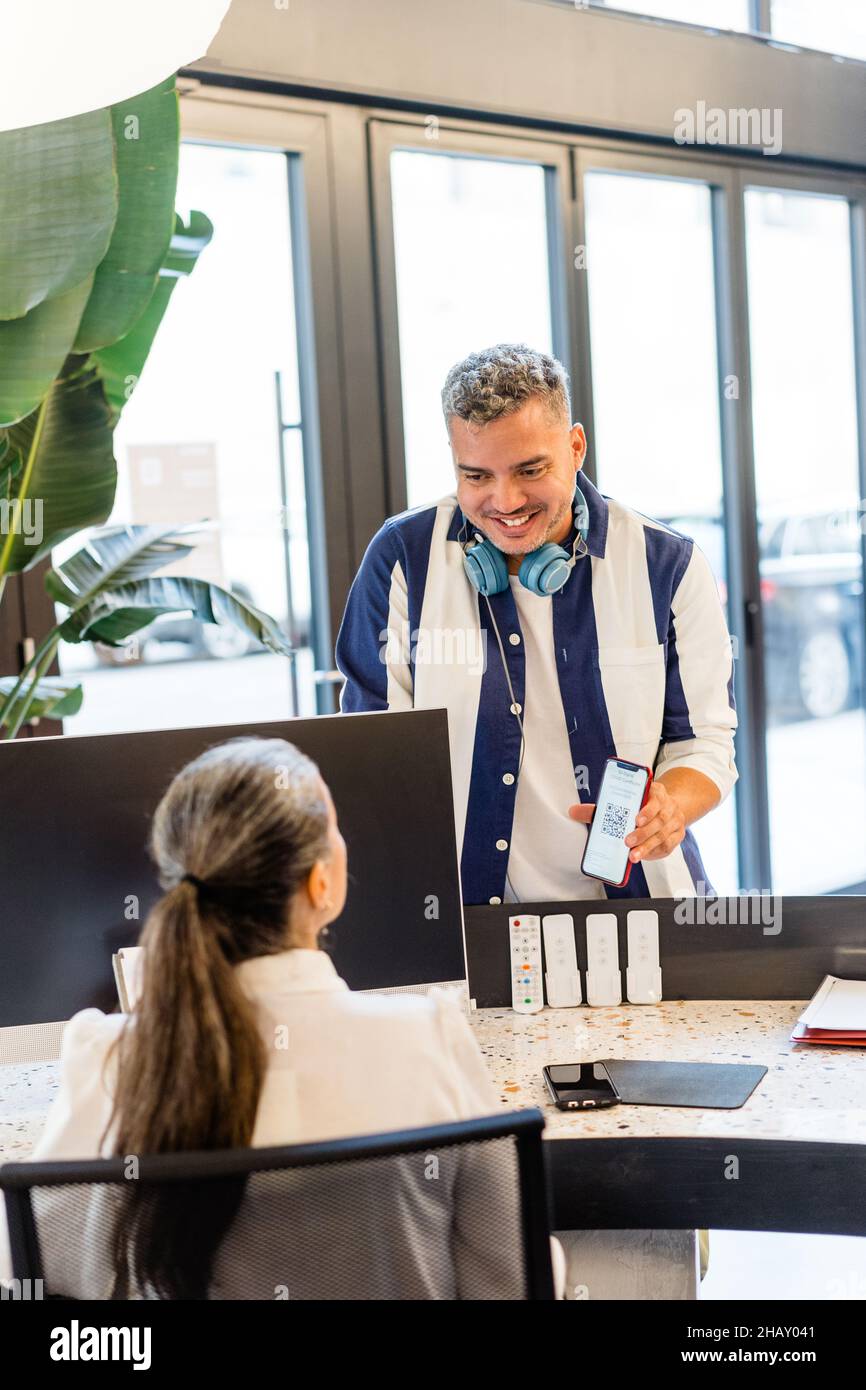 Positive male worker with headphones surfing cellphone near anonymous ...