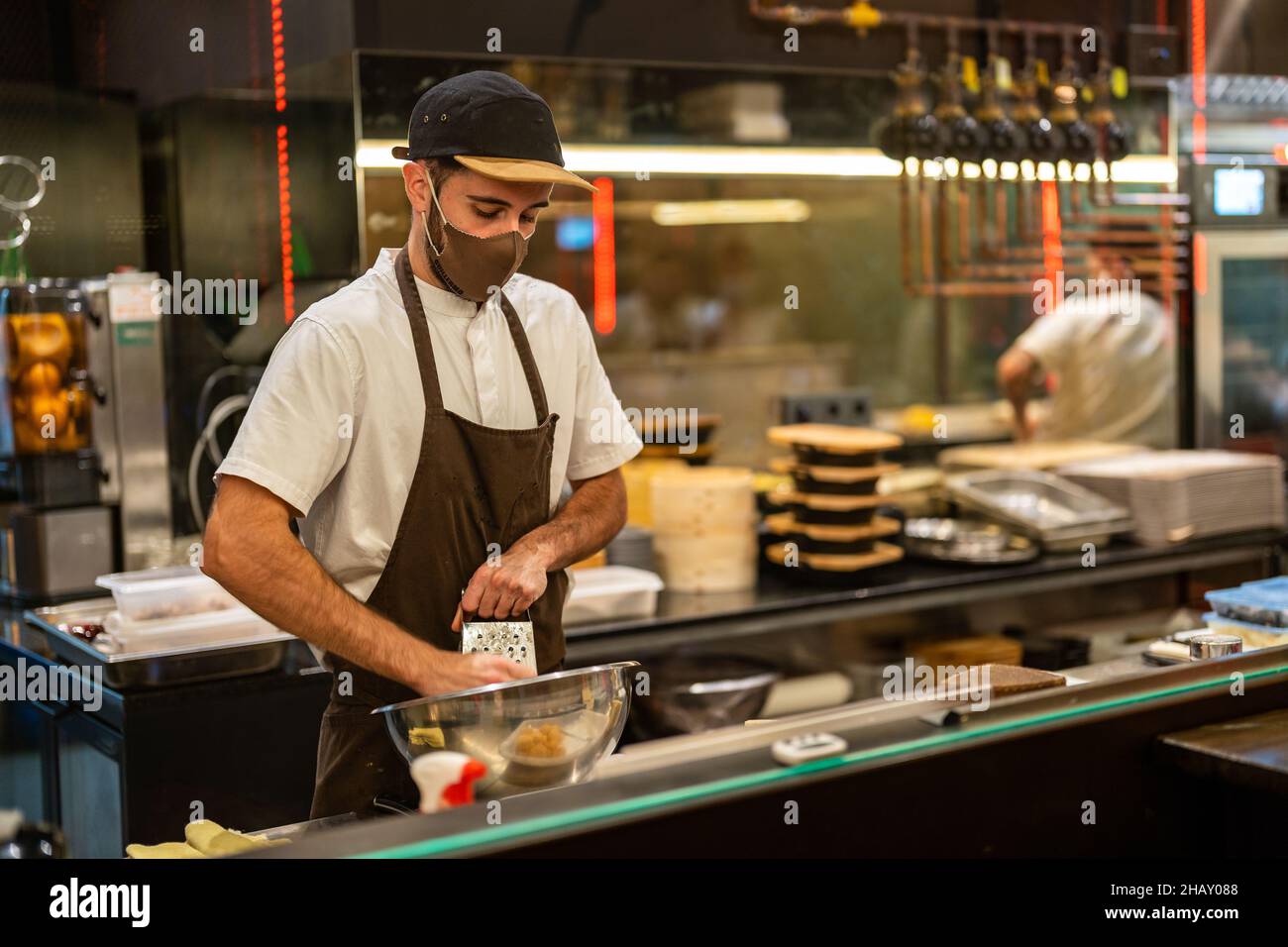 Through glass of focused young male cook in apron grating ingredient ...