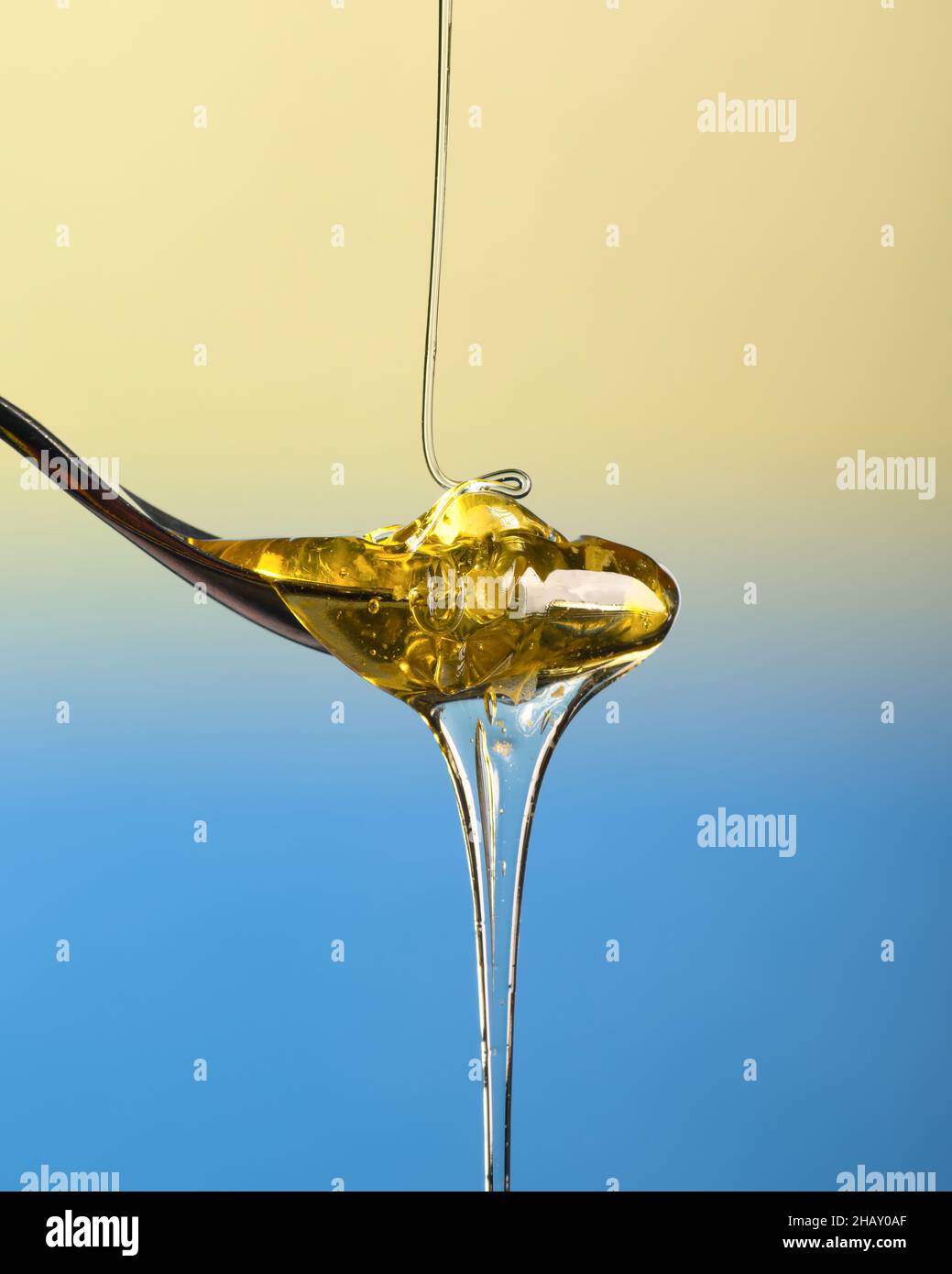 Stream of clear honey pouring onto a teaspoon and overflowing, isolated ...