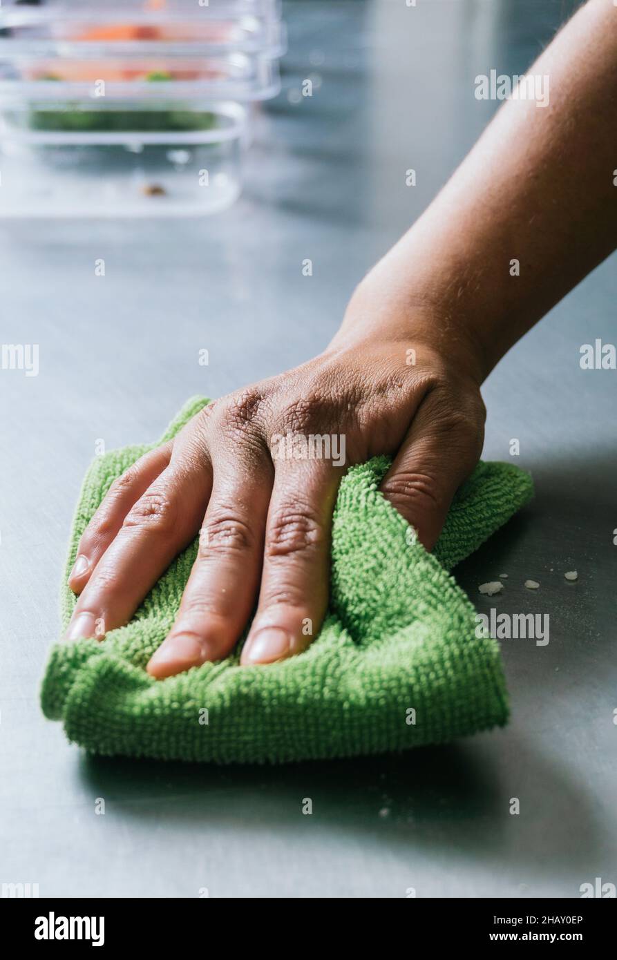 Crop unrecognizable female chef in uniform wiping off stainless steel ...