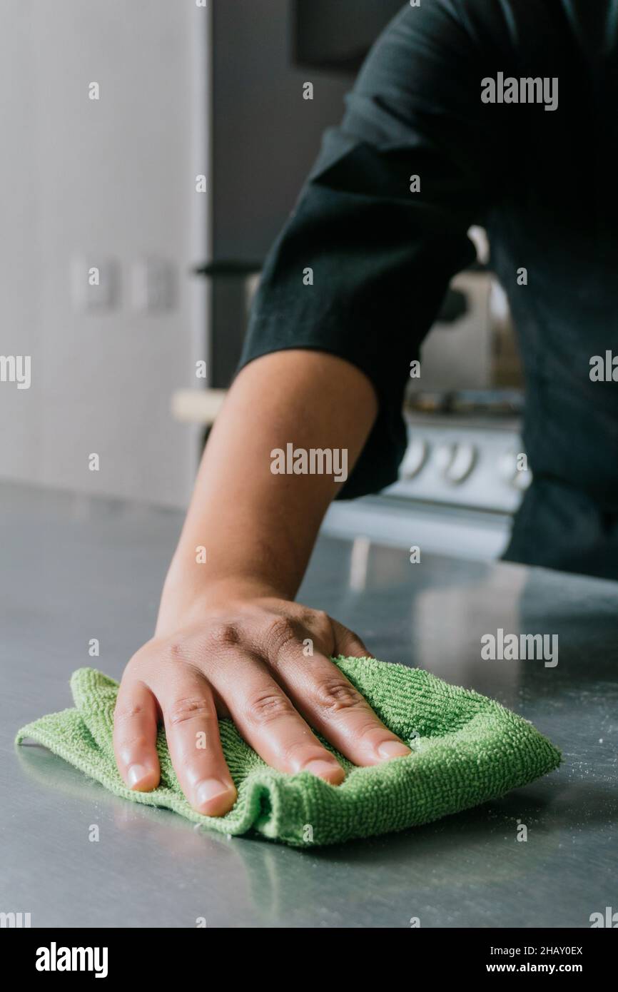 Crop unrecognizable female chef in uniform wiping off stainless steel ...