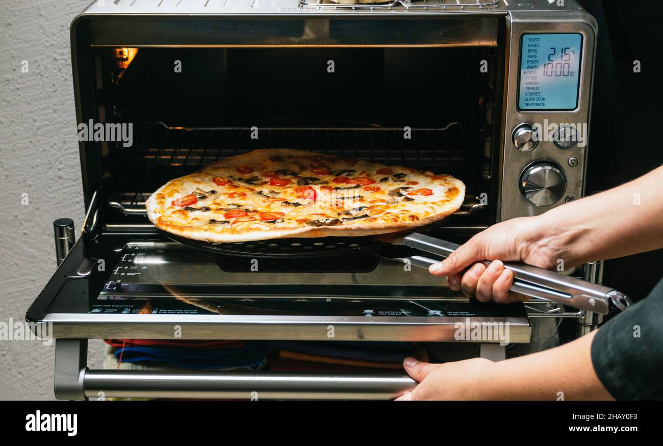 Crop anonymous female chef removing hot baked pizza with tomatoes and ...