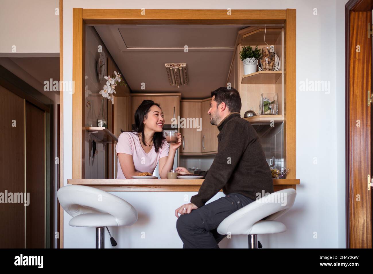 Positive multiracial couple with hot drinks looking at each other while ...