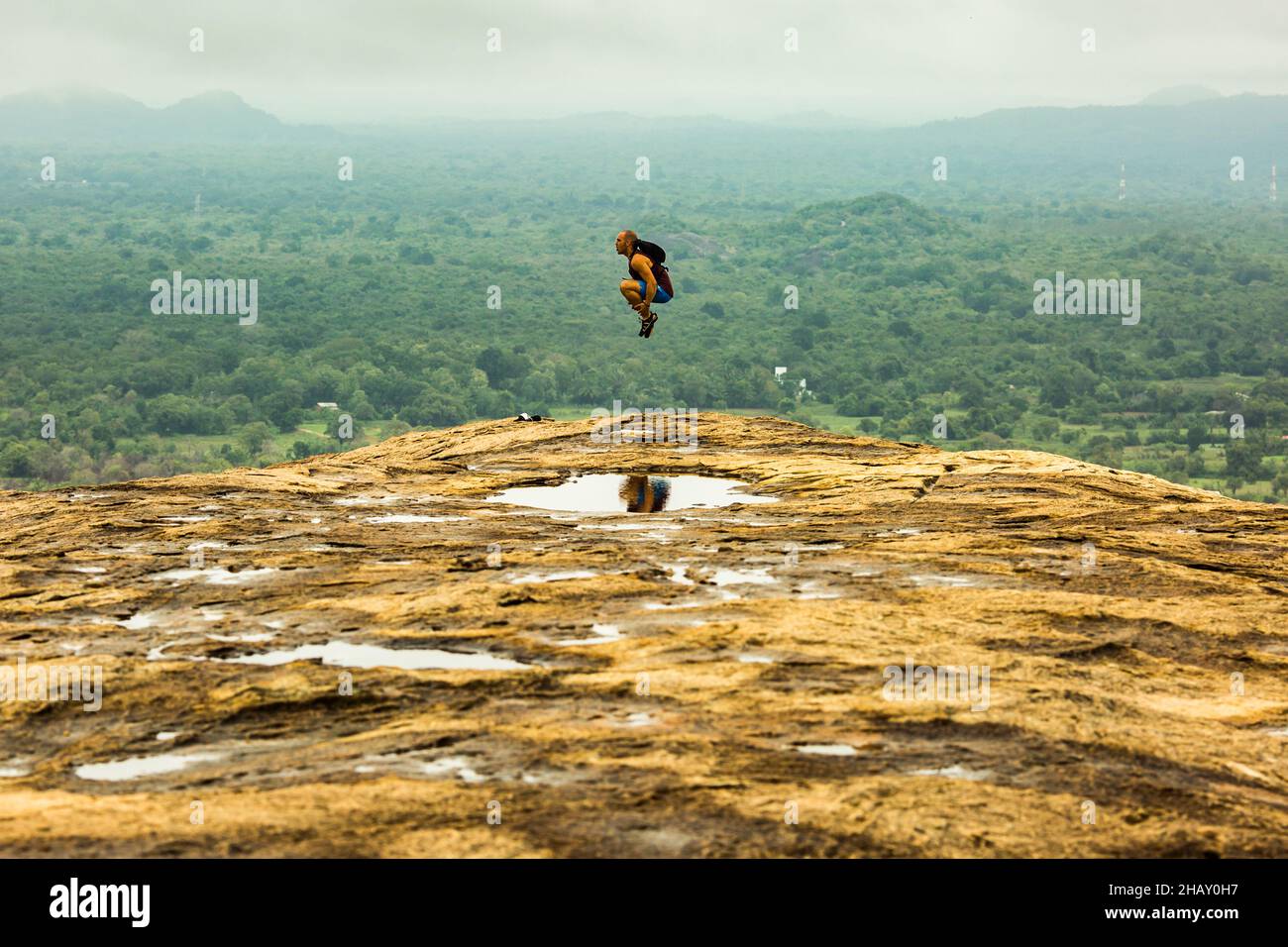 Side view of anonymous traveler jumping above puddle on mountain top ...