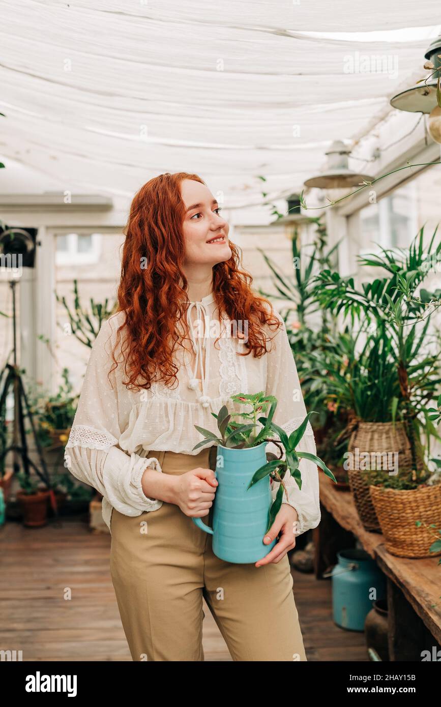 Charming female with long ginger hair standing with jug of seedling in ...