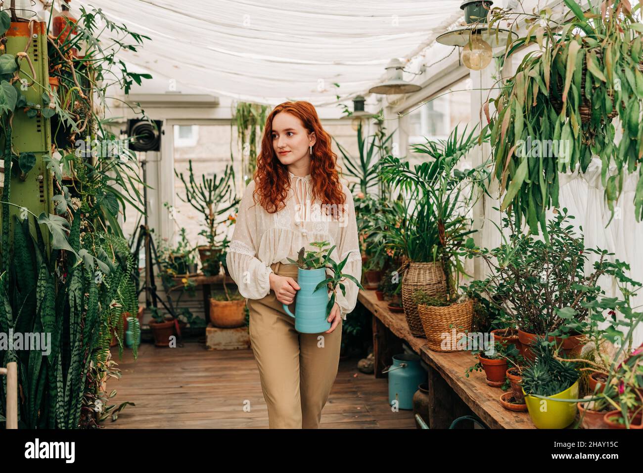 Charming female with long ginger hair standing with jug of seedling in ...