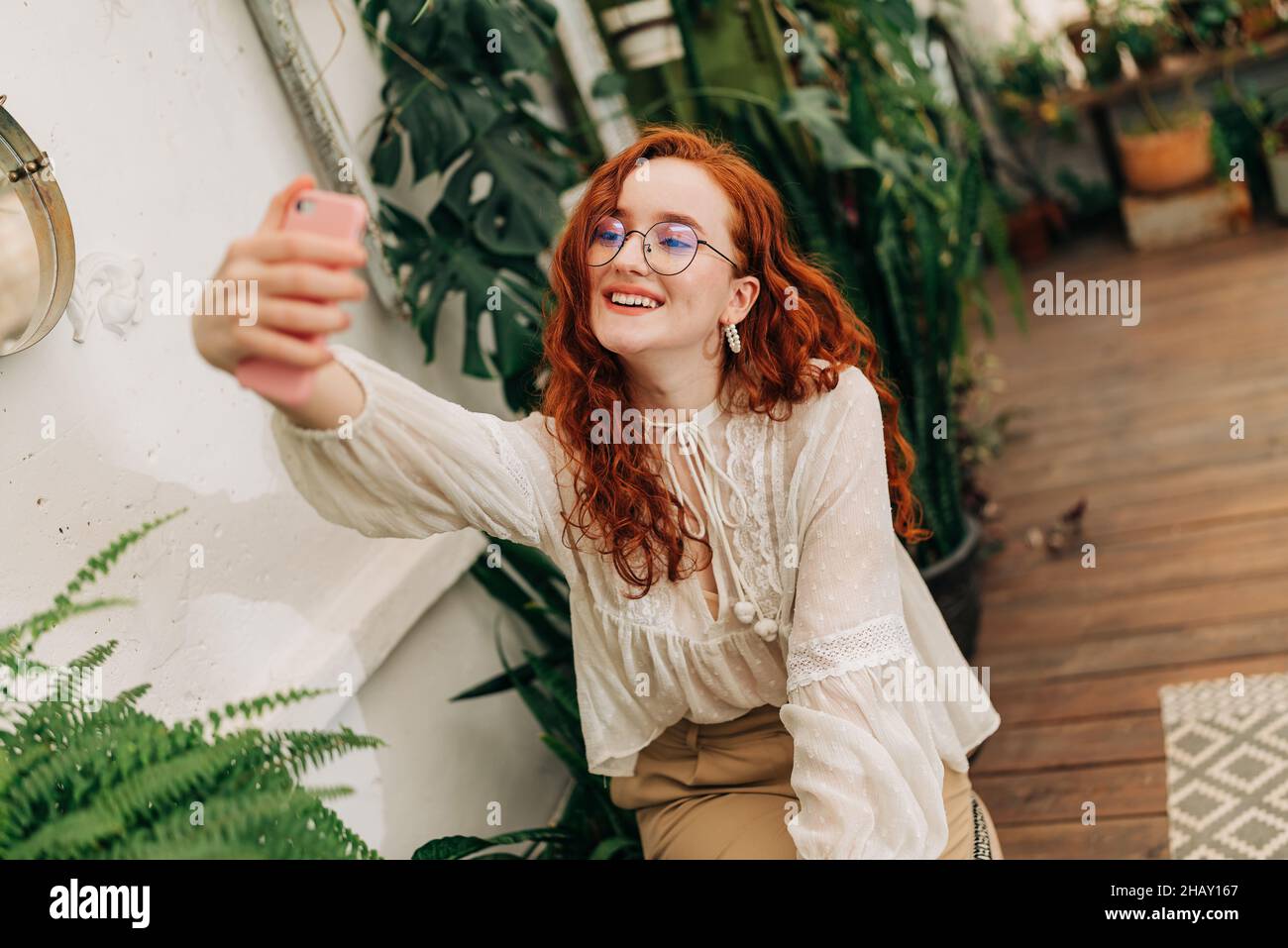 Smiling charming ginger haired female in eyeglasses sitting on chair ...