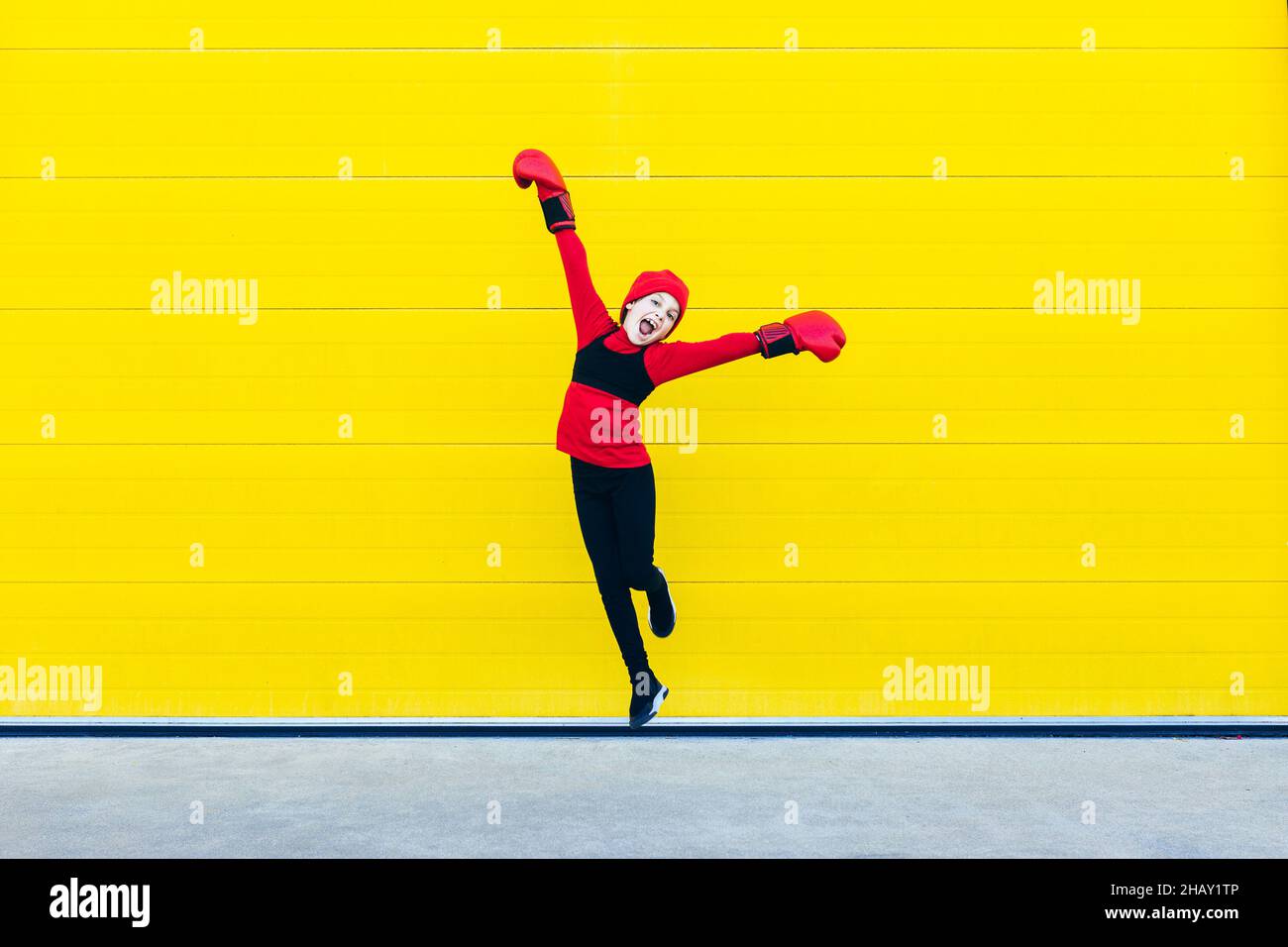 Full body of cheerful girl raising arms in boxing gloves and yelling ...