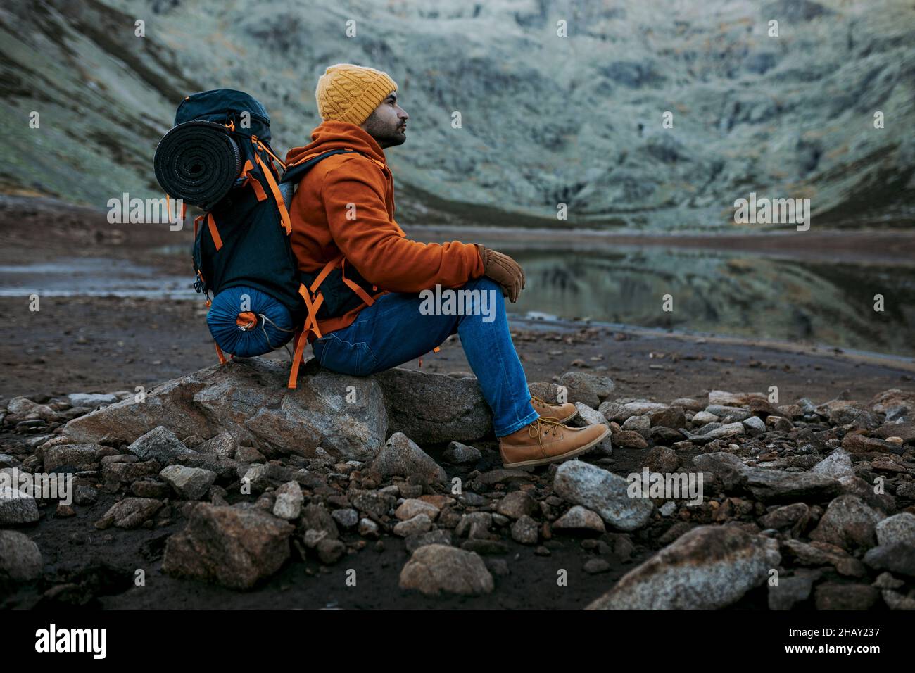 Full body side view of male traveler with backpack sitting on stony ...