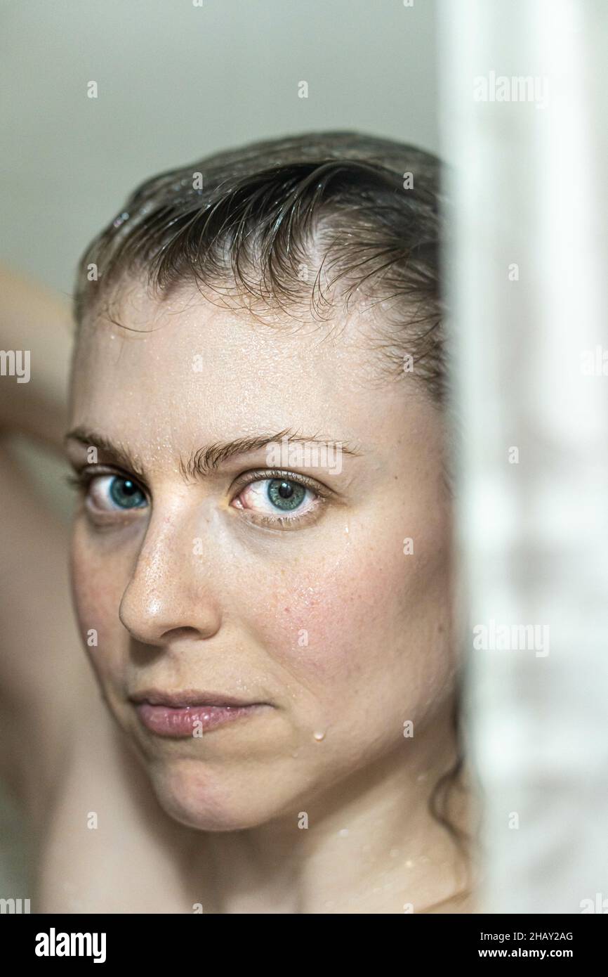 Portrait of a light blue-eyed Hispanic woman showering behind a shower ...