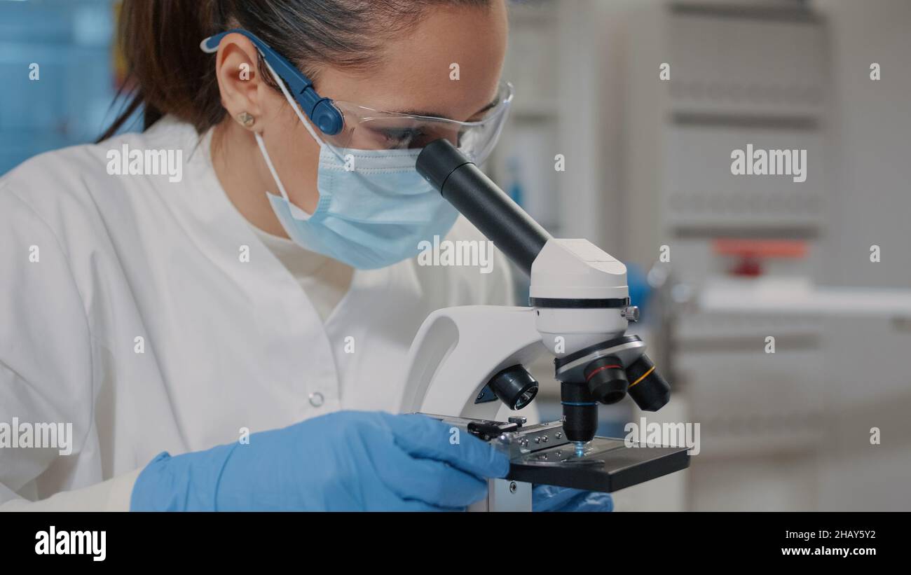 Biologist with face mask using microscope in science laboratory ...
