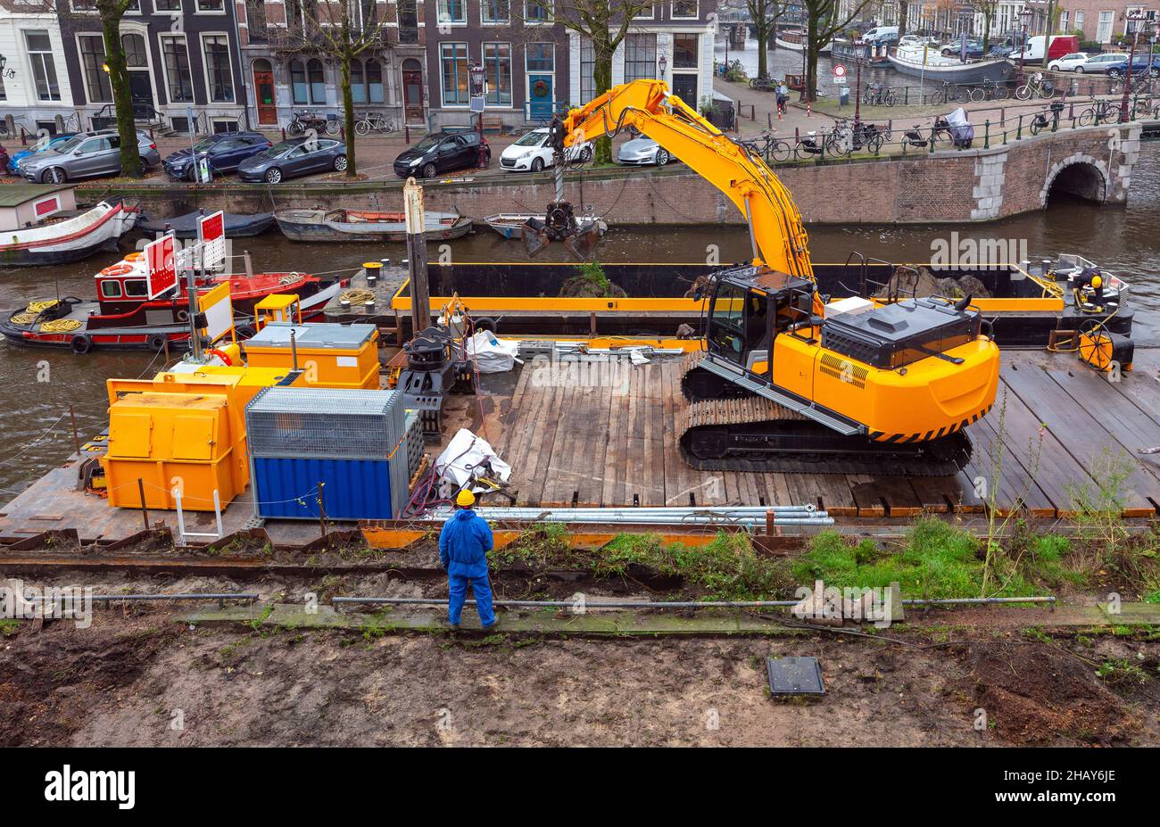 A large yellow excavator on a barge repairs the embankment. Amsterdam ...