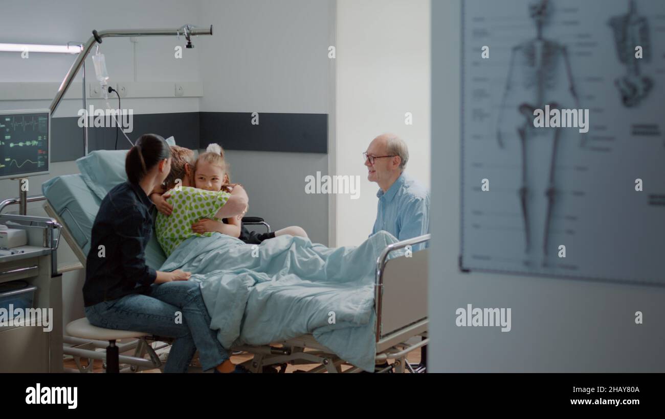 Child hugging sick patient in hospital ward bed at family visit with ...