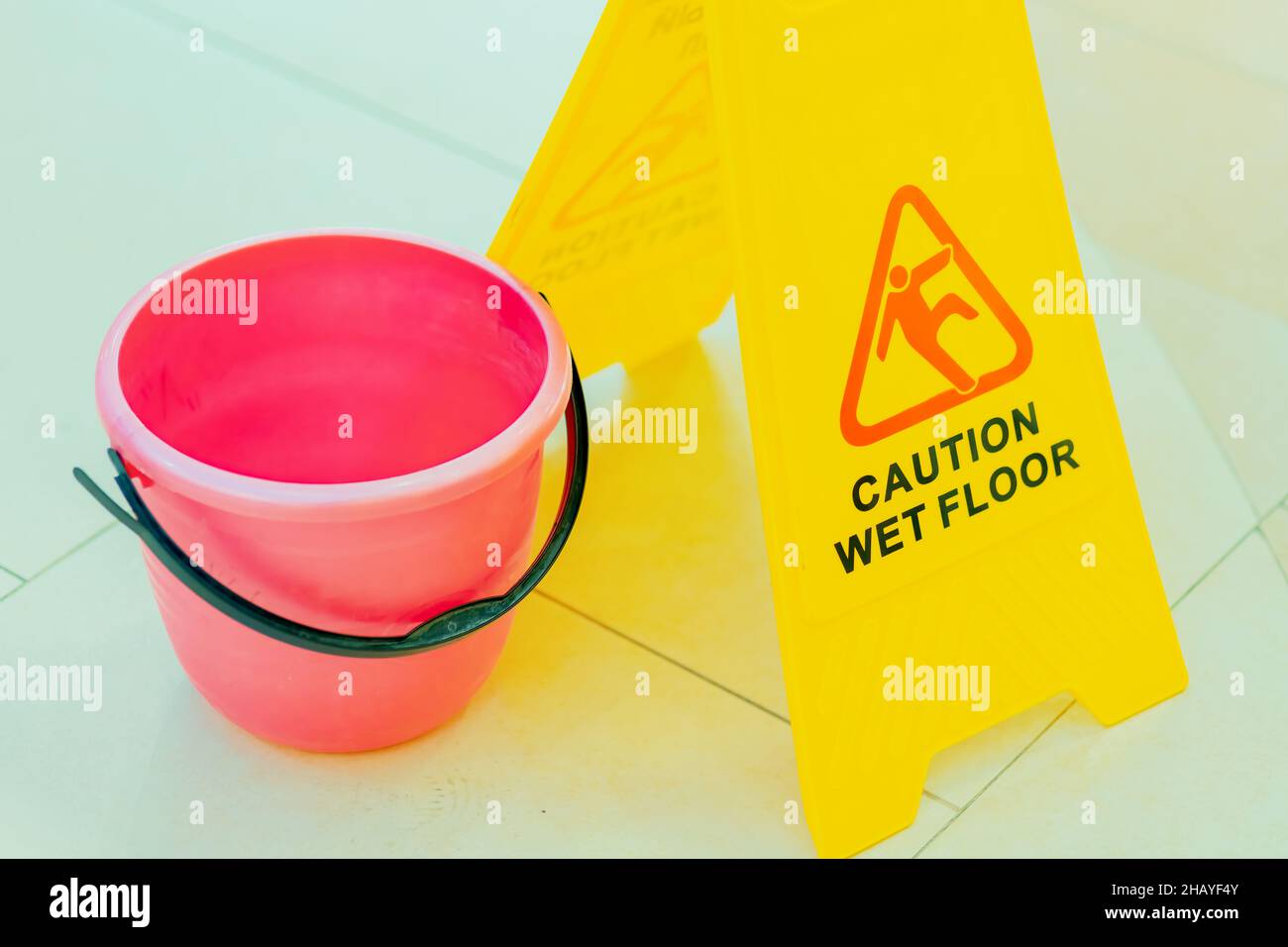 Yellow plastic warning sign that says caution wet floor and pink bucket ...