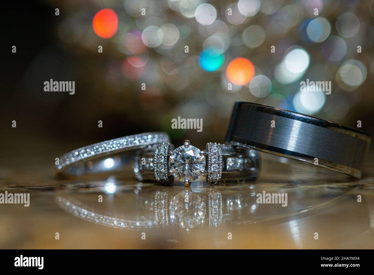 white gold wedding rings with diamonds reflecting on granite countertop and colorful bokeh ...