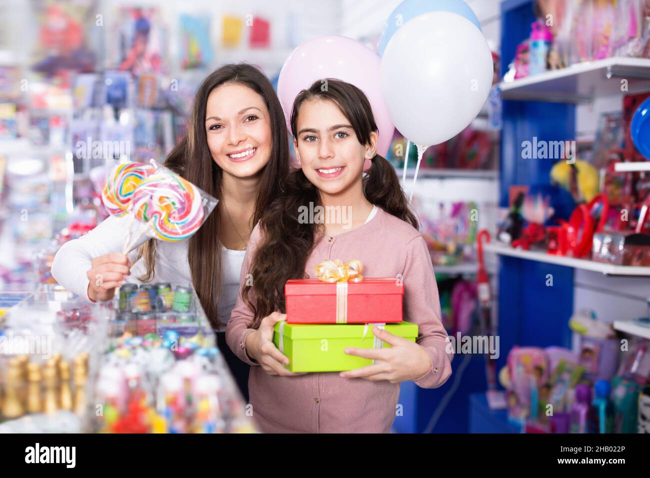 Smiling female and girl with gifts and balloons in the candy store ...