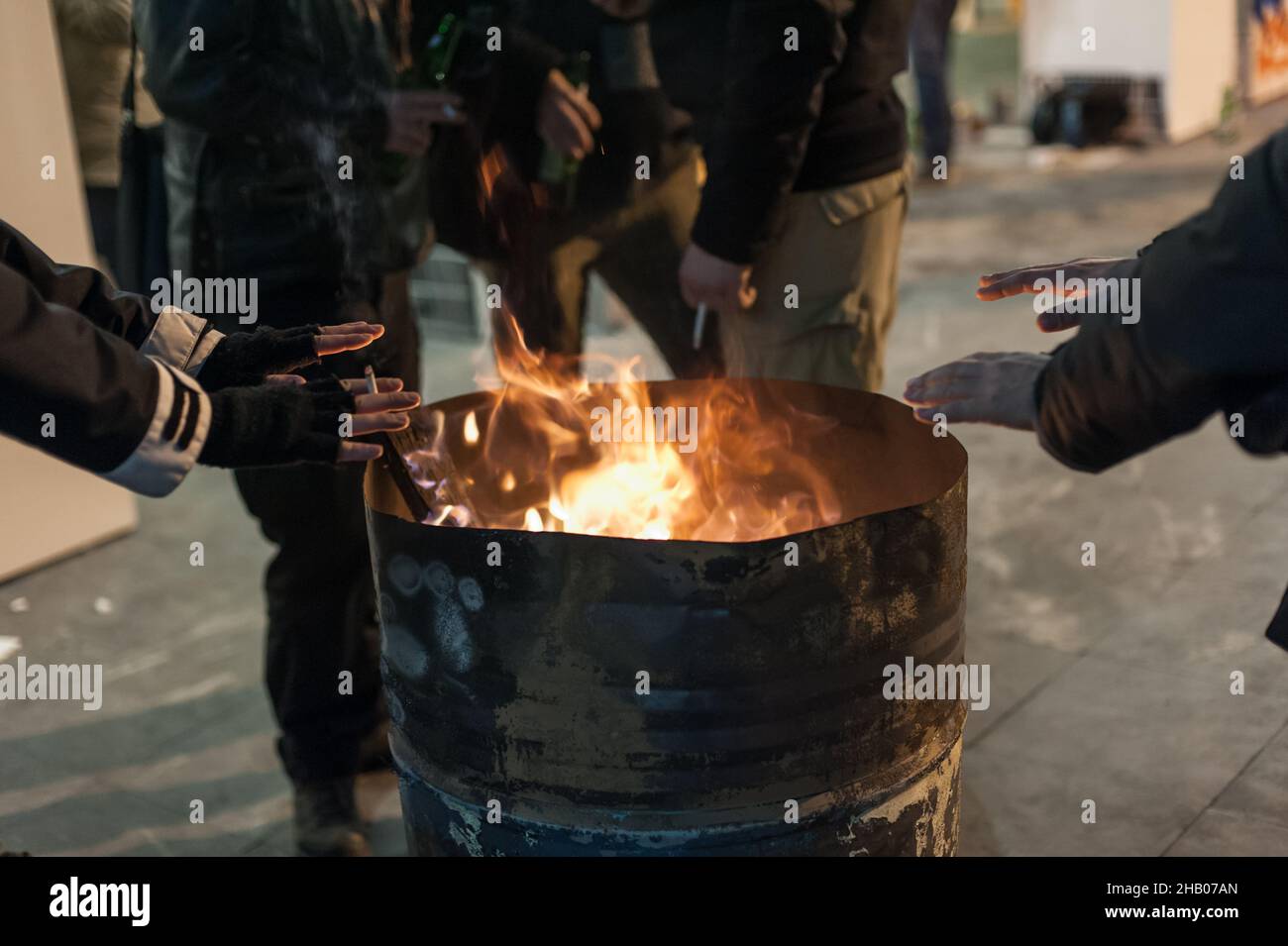 Homeless man warming his hands by a fire. Poor men warm outdoors near ...