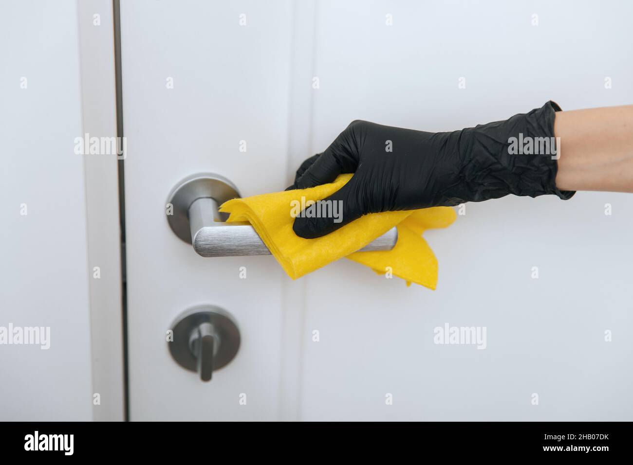 Cleaning door handle with yellow wipe in black gloves. Woman hand using ...
