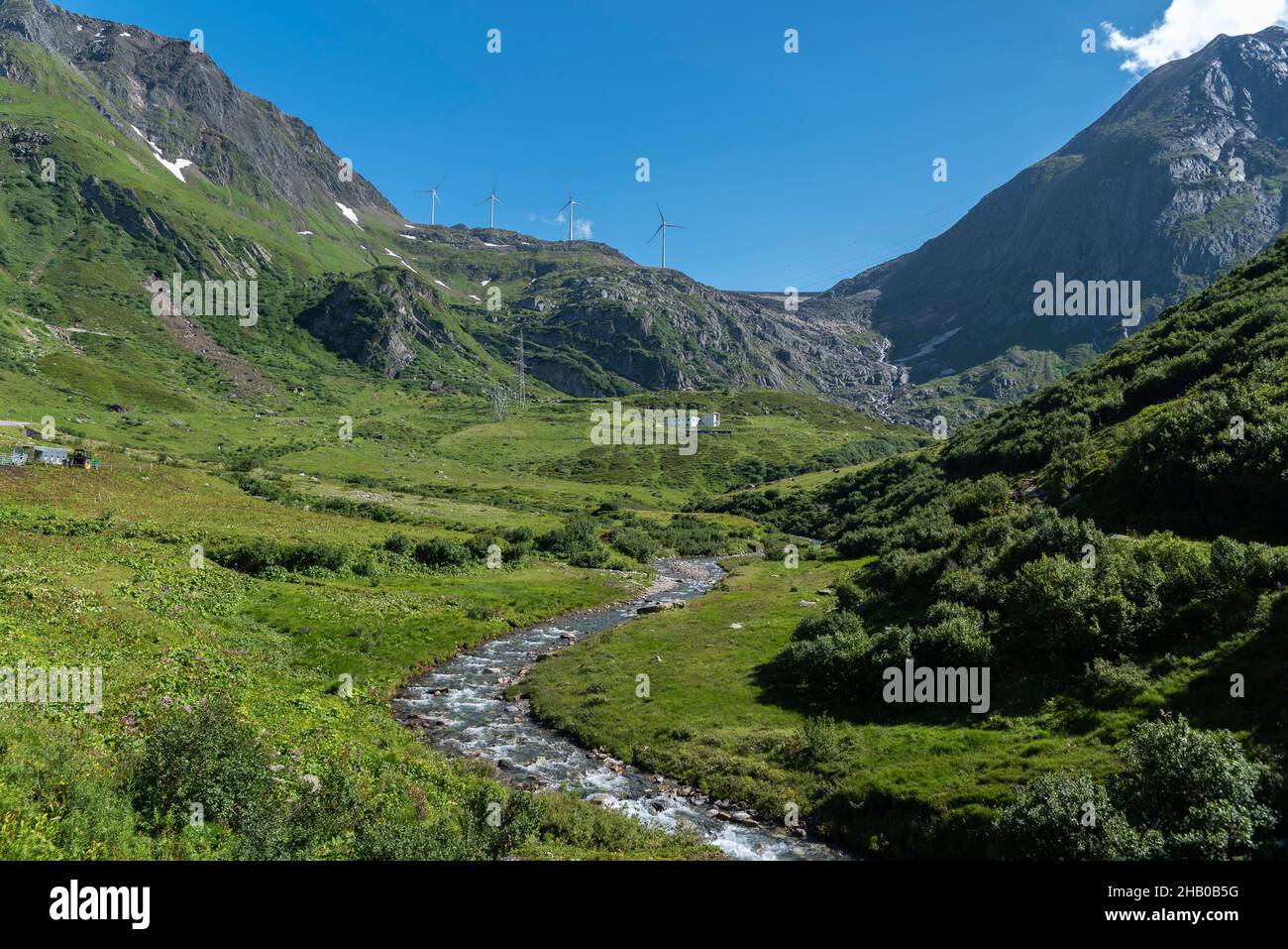 Alpine landscape along the Nufenenpass road with a wind turbine below ...
