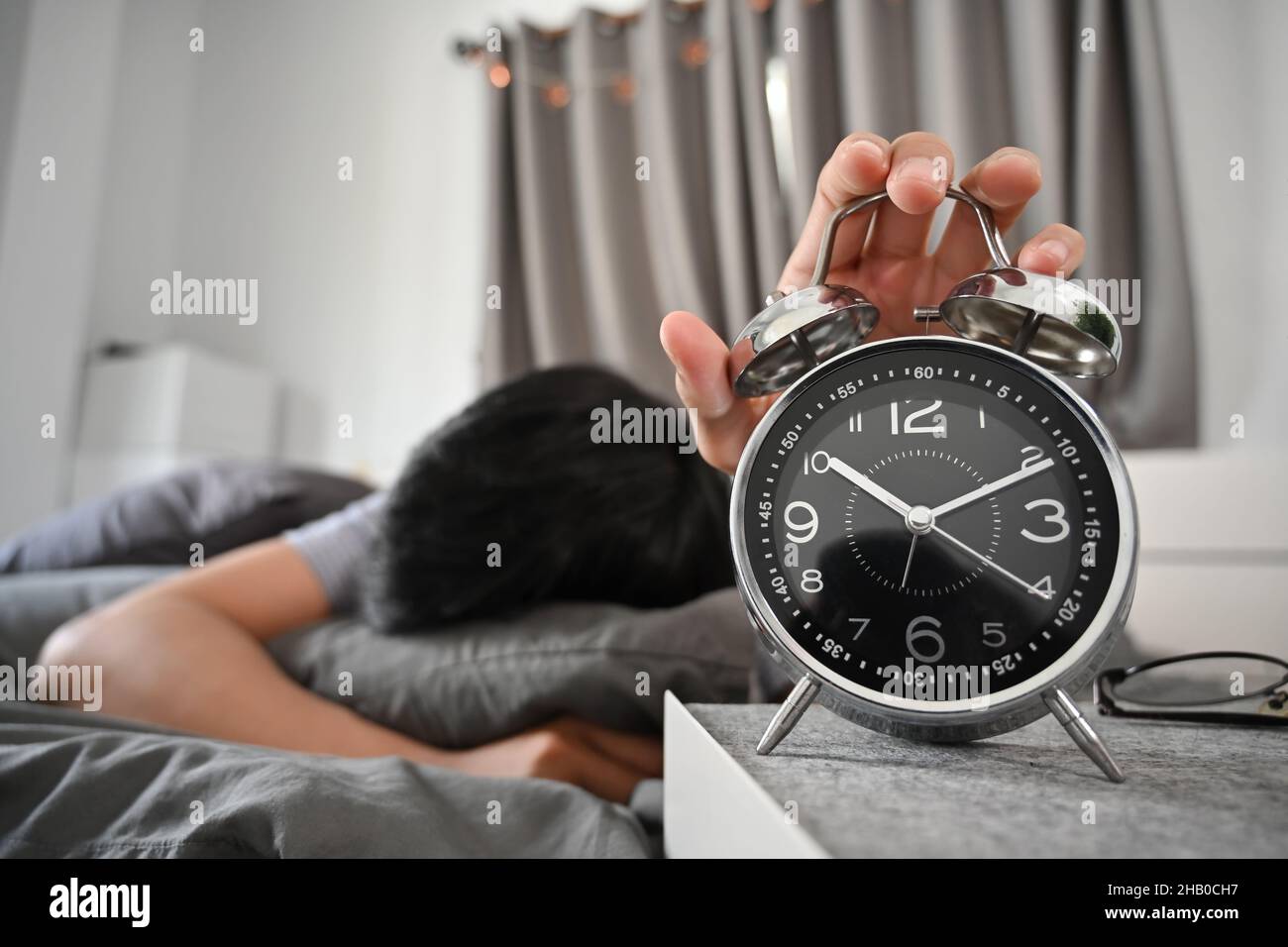 Young Man Lying On Bed And Turning Off An Alarm Clock In The Morning