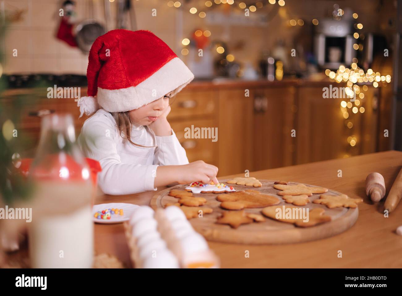 Little girl in santa hat decorates gingerbread using multicolored beads ...