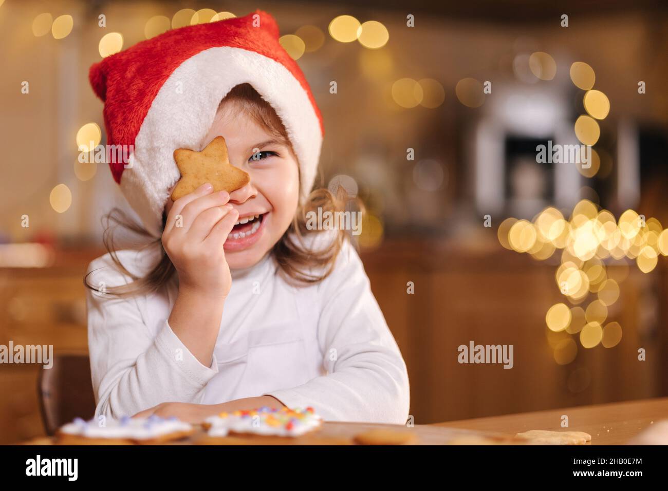 Adorable little girl in santa hat close one eye by gingerbread and ...