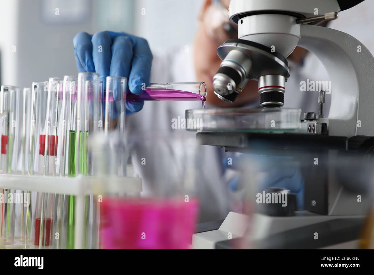 Female scientist pouring pink sample liquid on glass container under ...