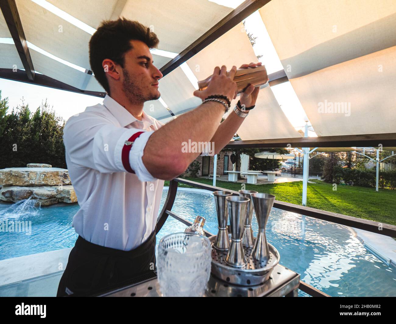 Young attractive Caucasian barman shaking a cocktail at an outdoor ...