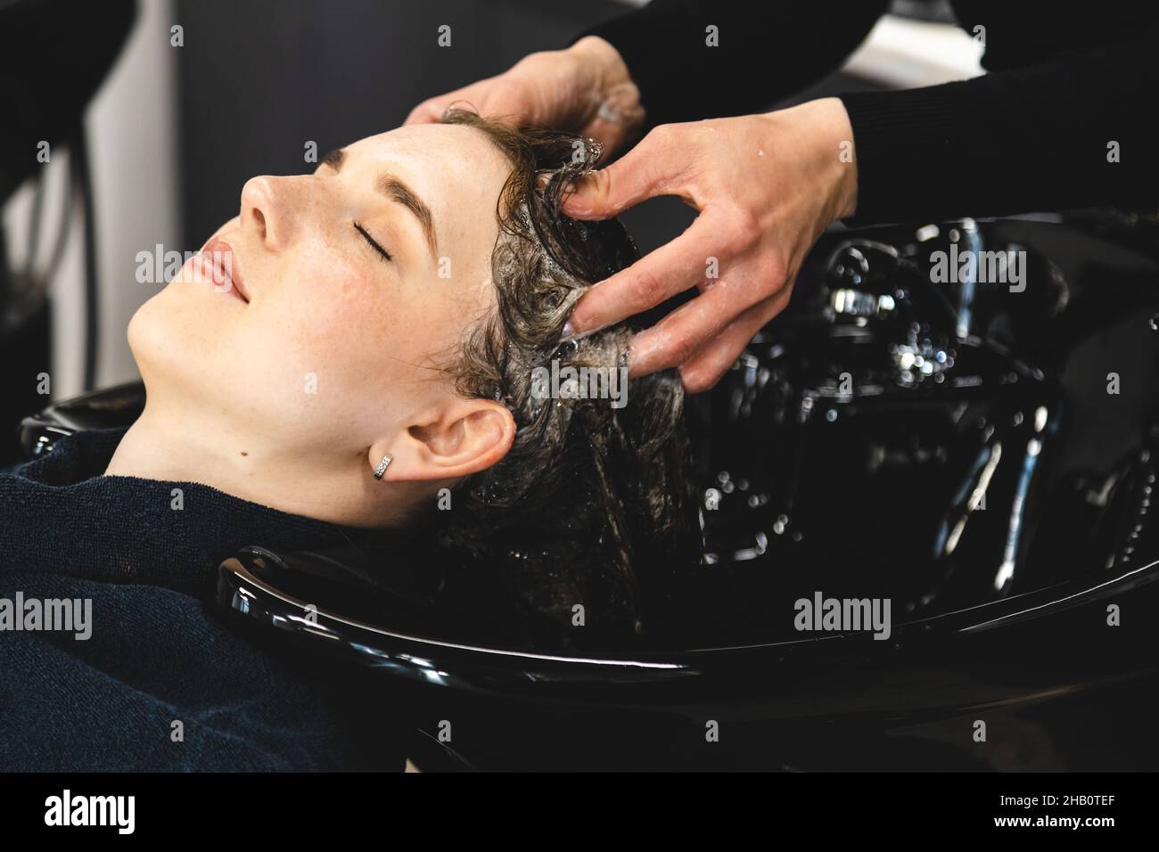 Master woman hairdresser gently washes the girl's hair with shampoo and ...