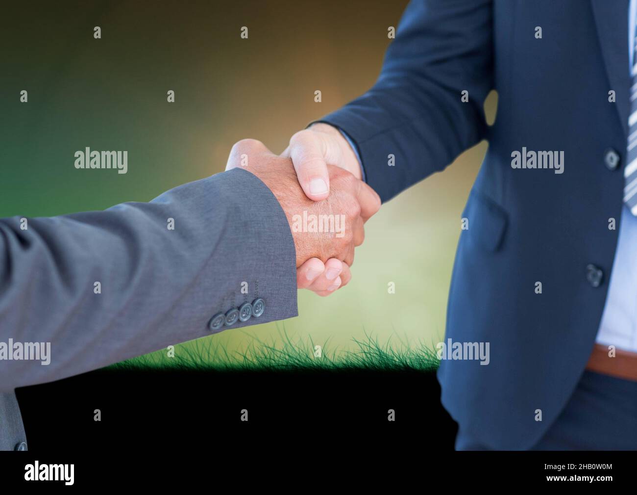 Mid section of two businessmen shaking hands against grass in ...