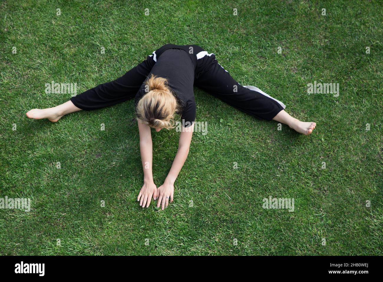Young woman doing stretching exercises while lying on the green grass ...