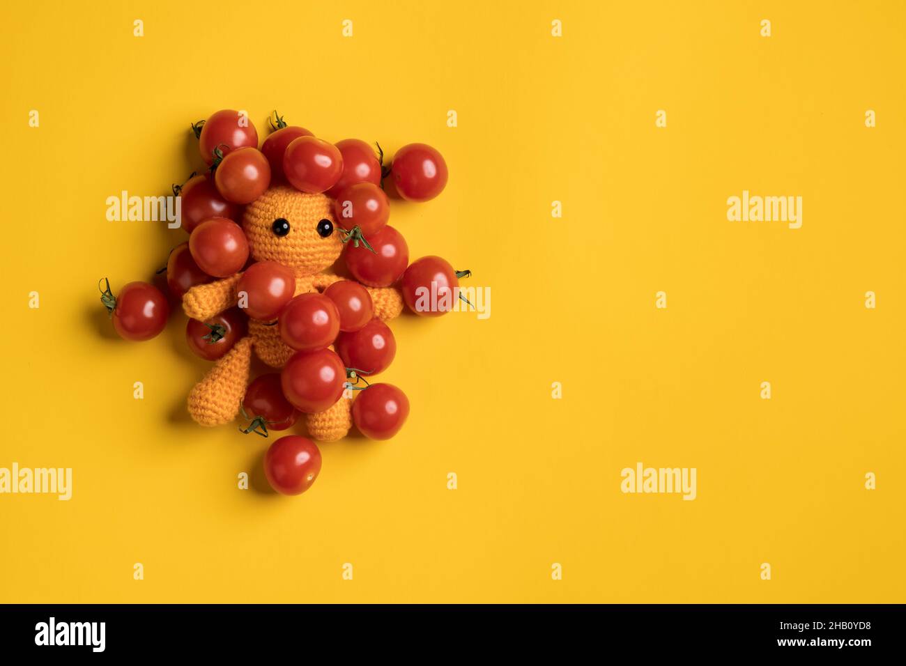 Cute homemade knitted toy man in red cherry tomatoes, on a yellow ...