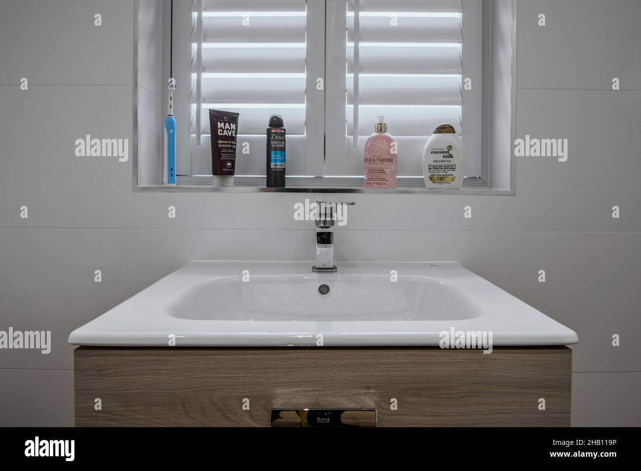 White bathroom sink with various toiletries etc on the window ledge ...