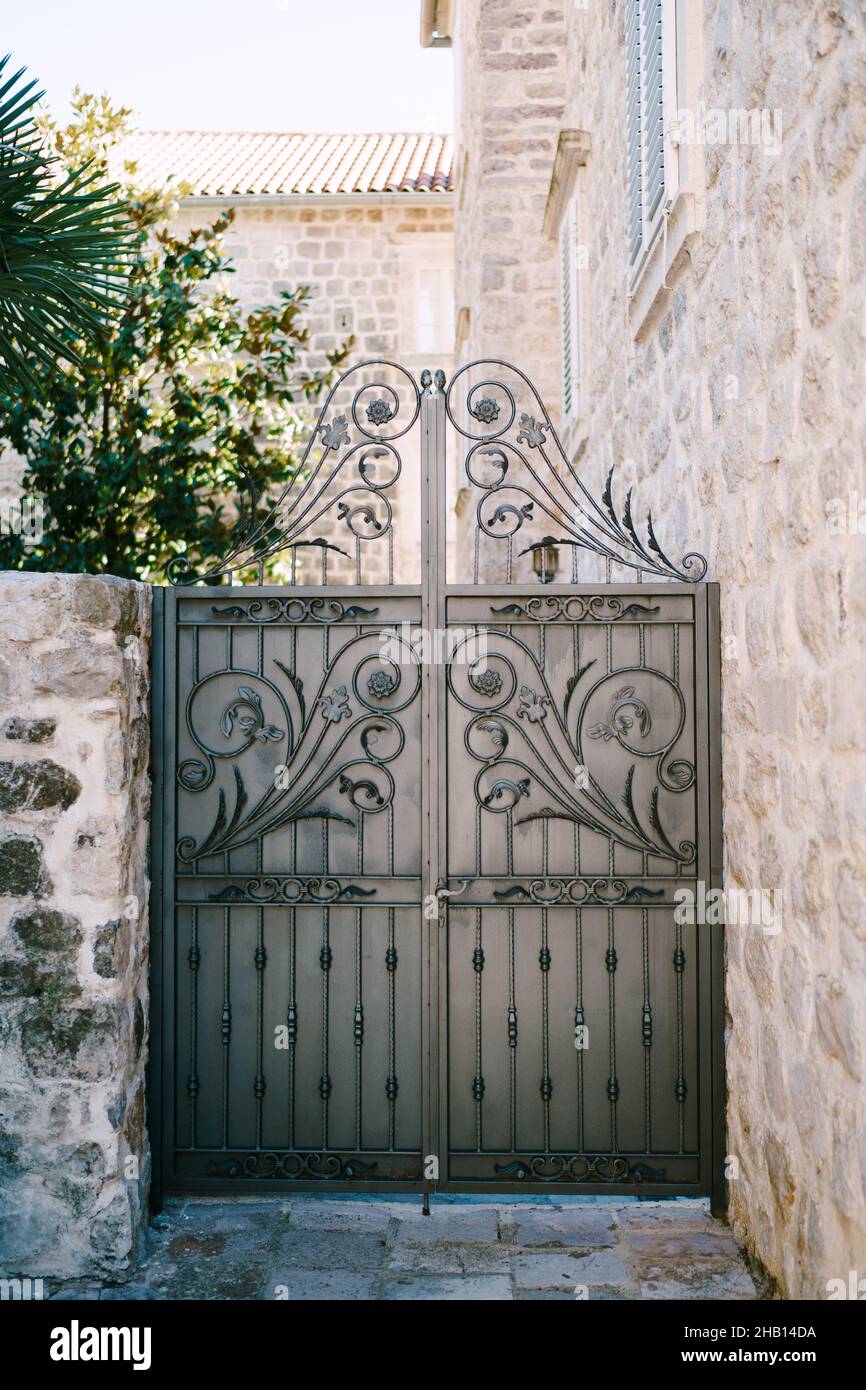 Forged openwork gate near the wall of a stone house with shutters Stock ...