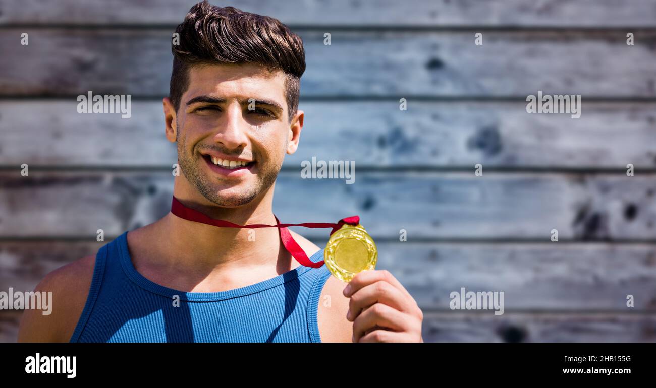 Composite image of caucasian male athlete holding a gold medal against ...