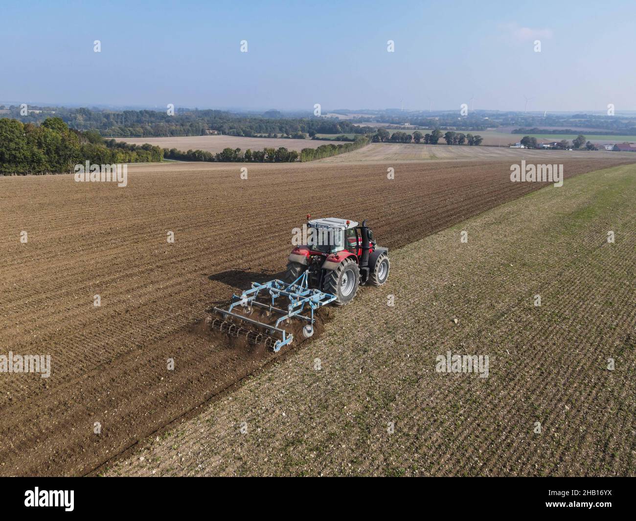 Aerial view of a farmer and tractor turning over soil with a harrow in ...