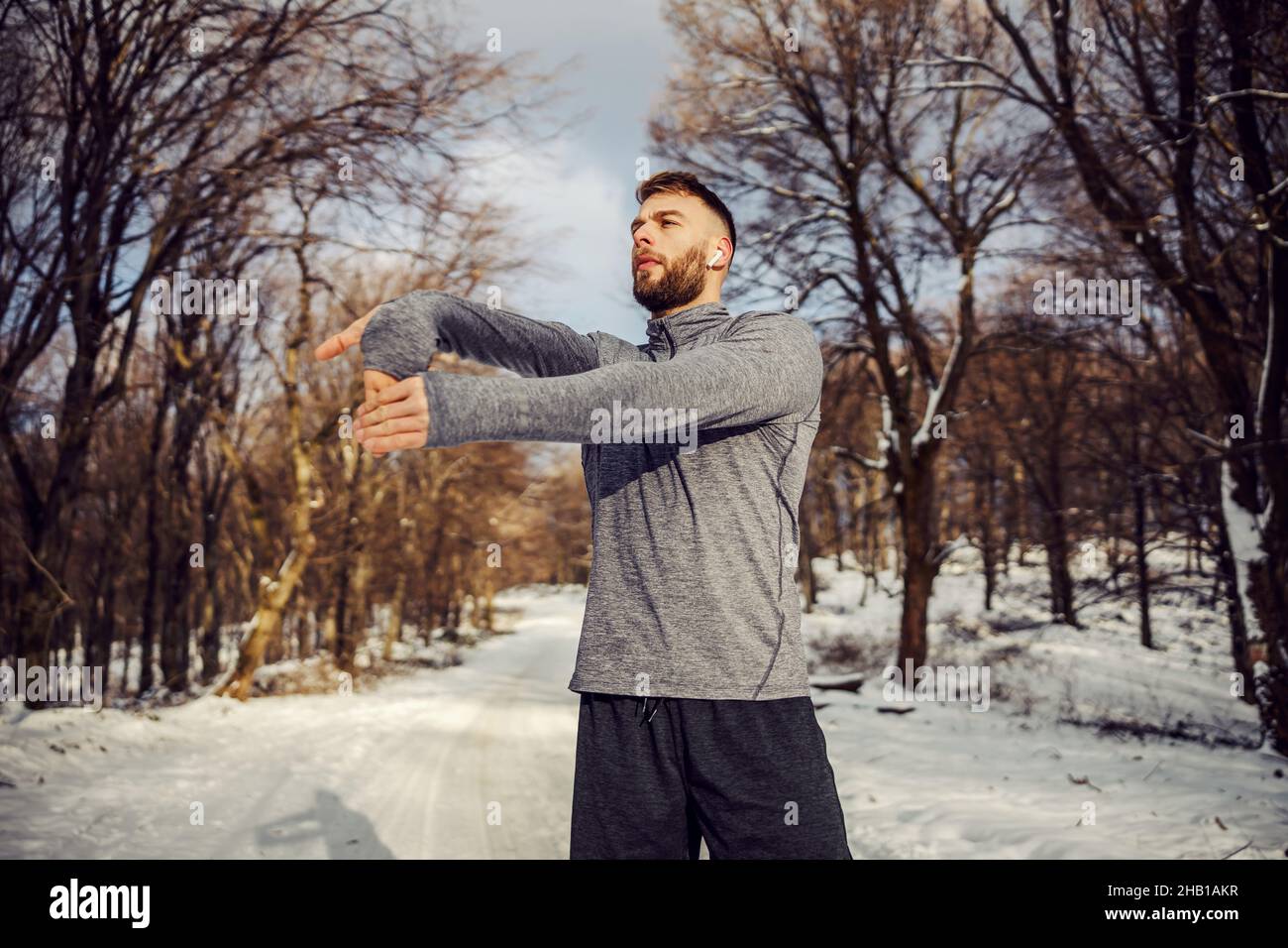 Sportsman standing in nature and doing warm up exercises at snowy ...