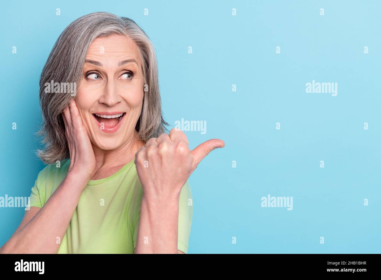 Photo of amazed positive old woman point finger empty space hold hand ...