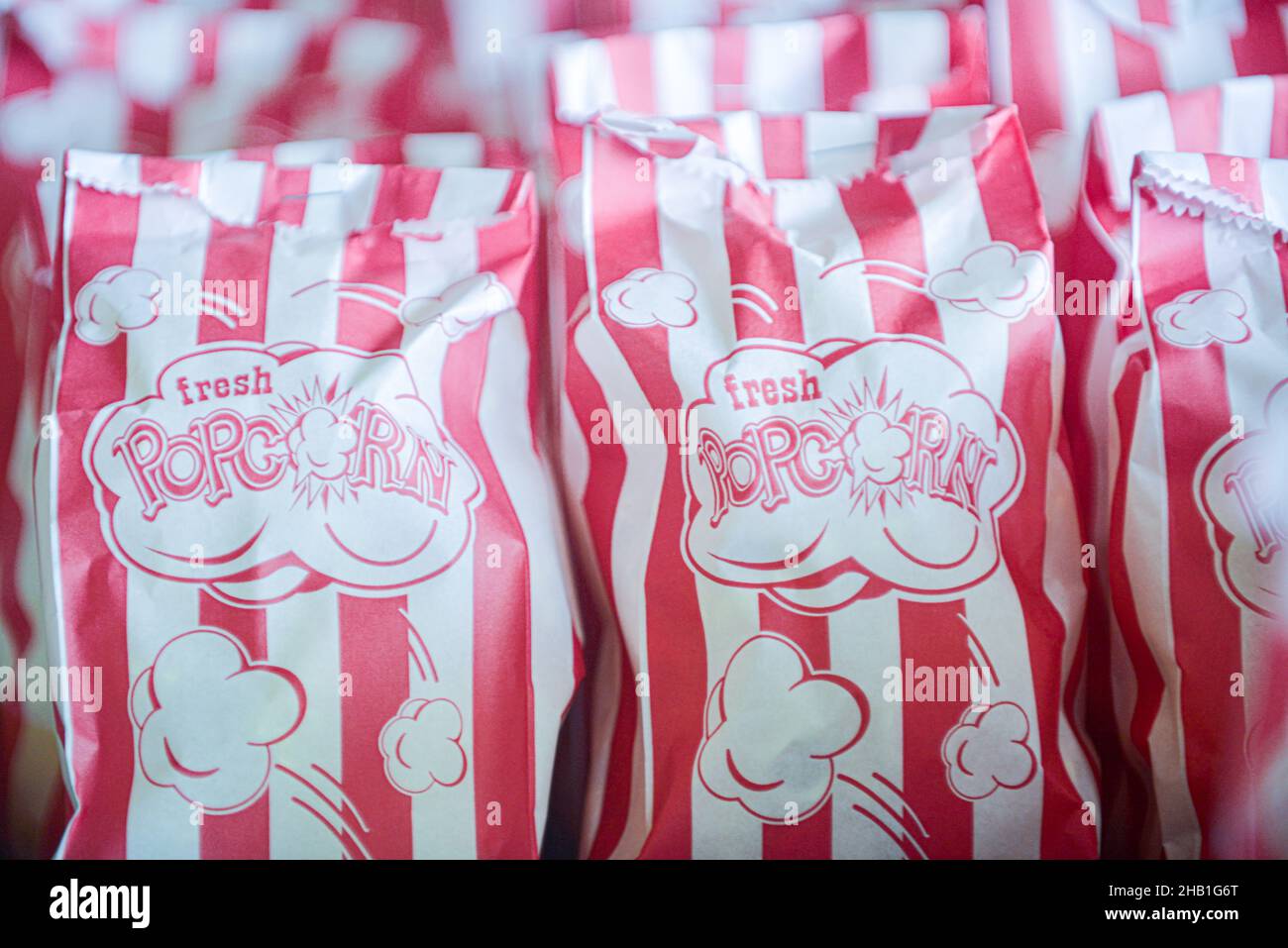 Many rows of popcorn in white paper bags with red vertical stripes and ...