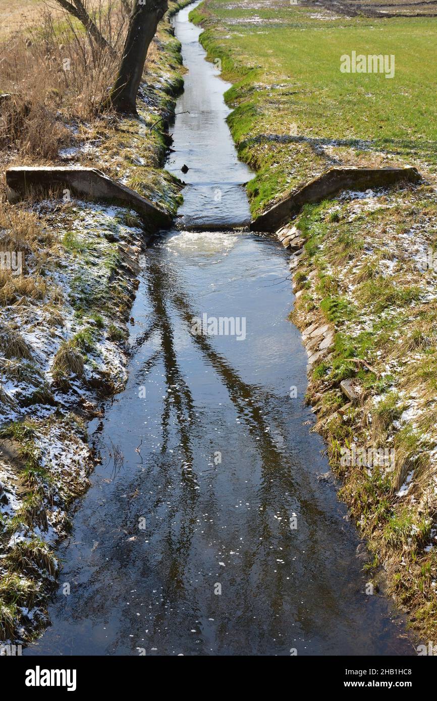A small stream divided by a concrete dam, a sunny spring day. Water ...
