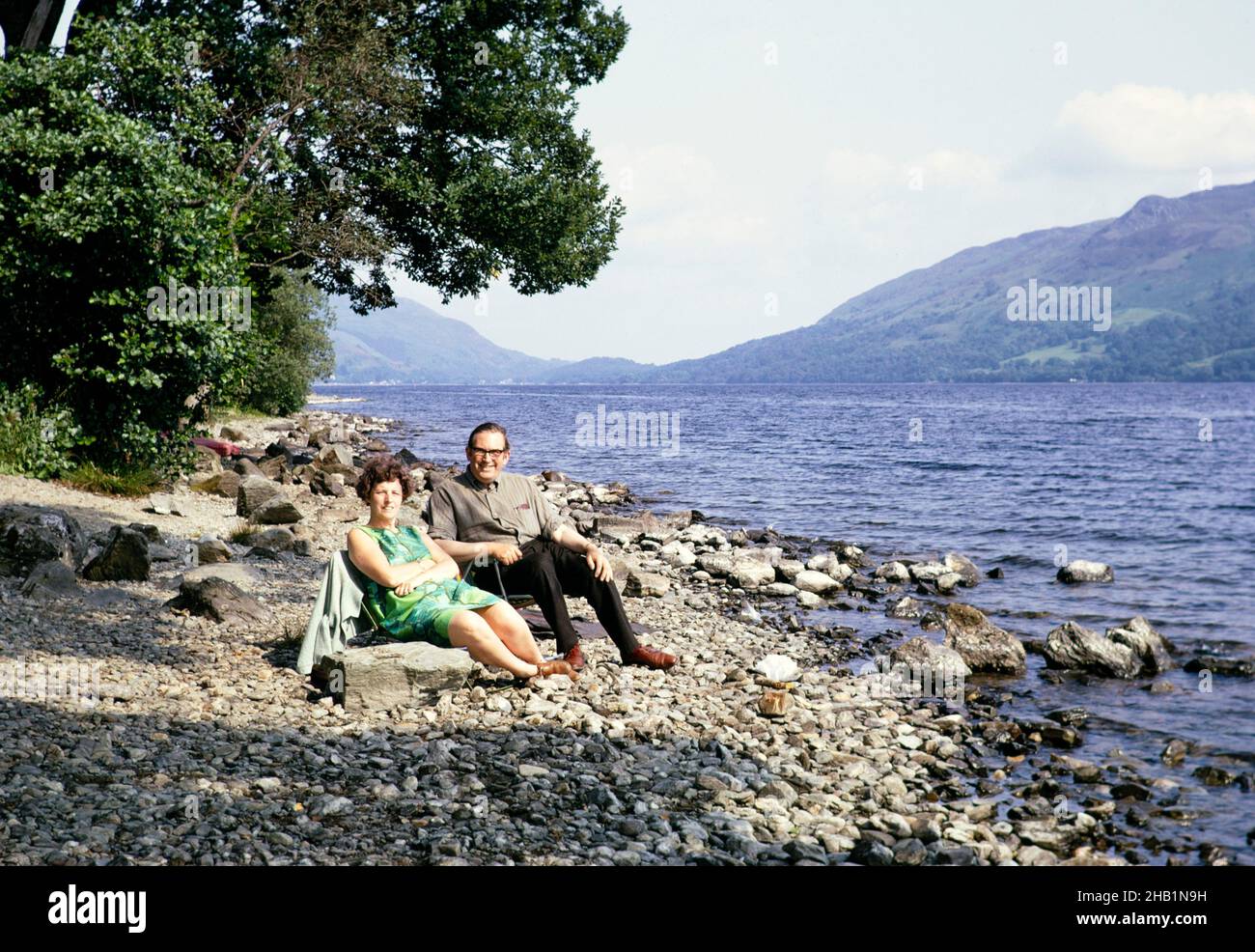 Man and woman sitting on beach at Loch Earn lake , Perthshire, Scotland ...