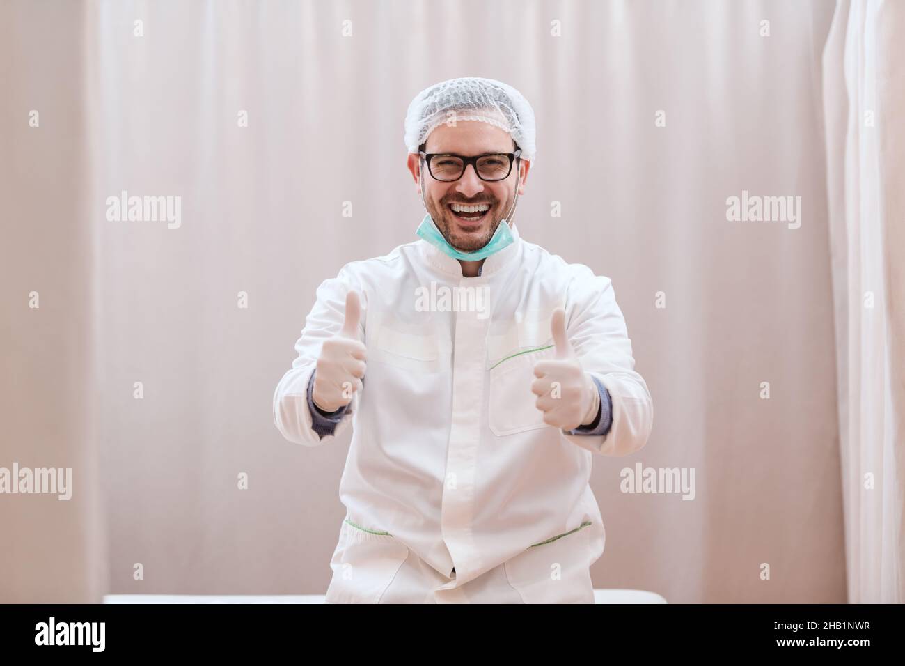 Happy surgeon in sterile uniform showing thumbs up and smiling ...