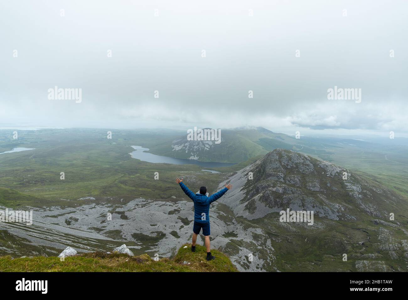Man standing on top of mountain raising his arms in Errigal mountain Co ...