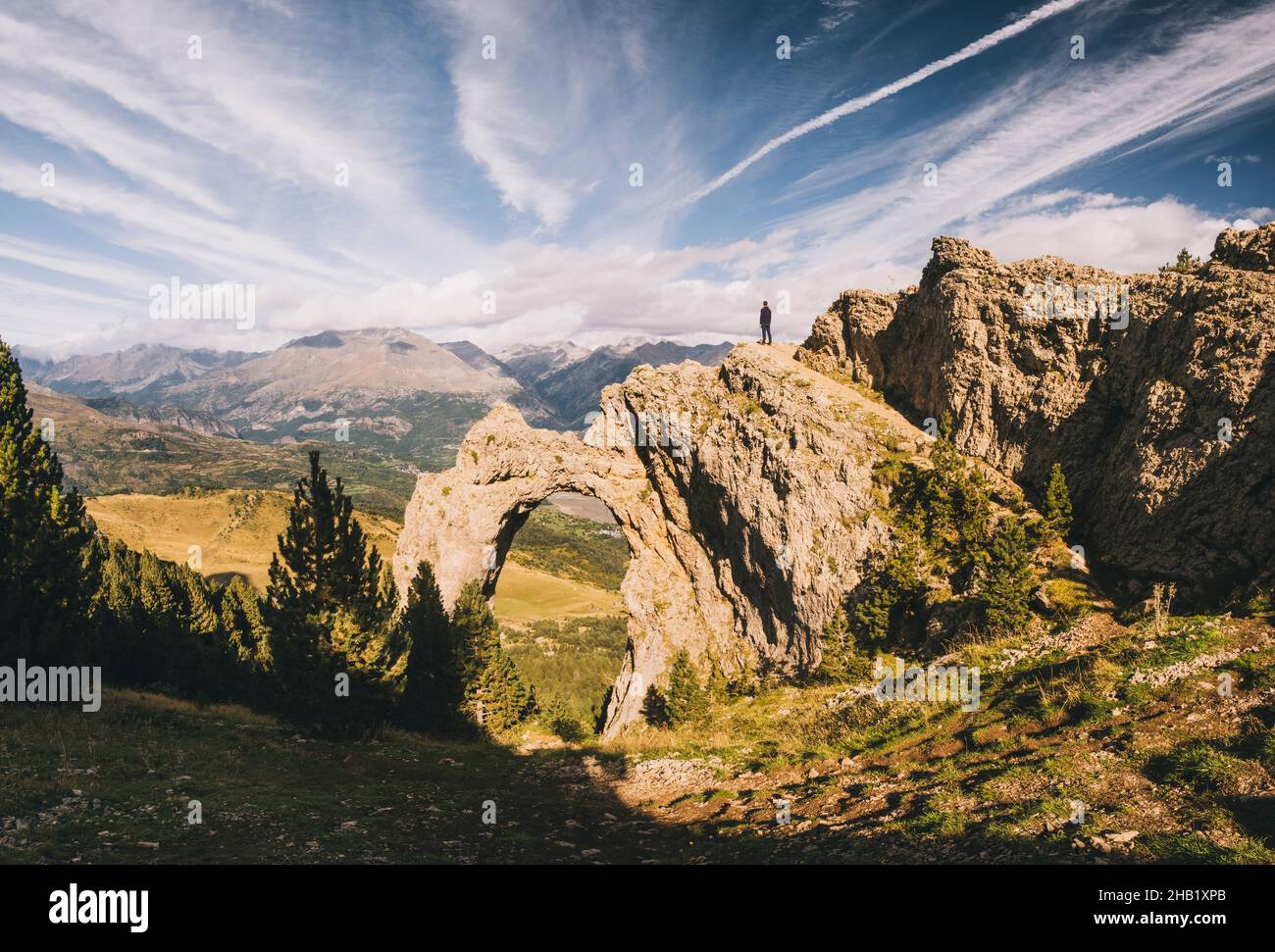 Happy man on top of an arch rock formation against high mountains ...