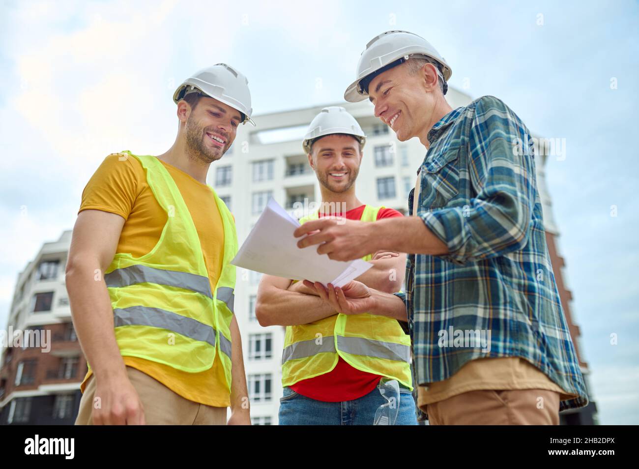 Three men with drawing discussing at construction site Stock Photo - Alamy